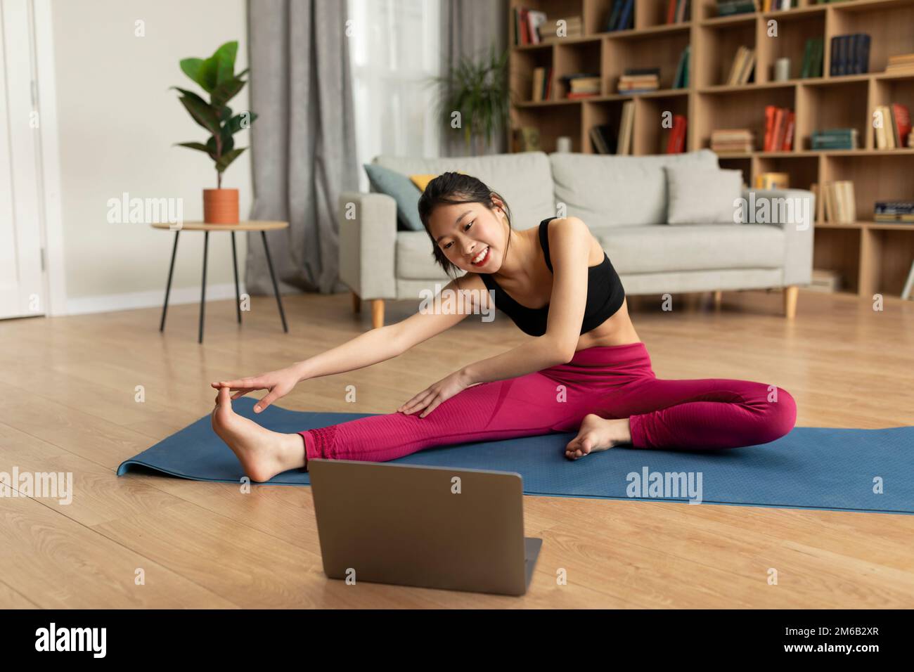 Home training. Young japanese lady stretching leg muscles in front of ...