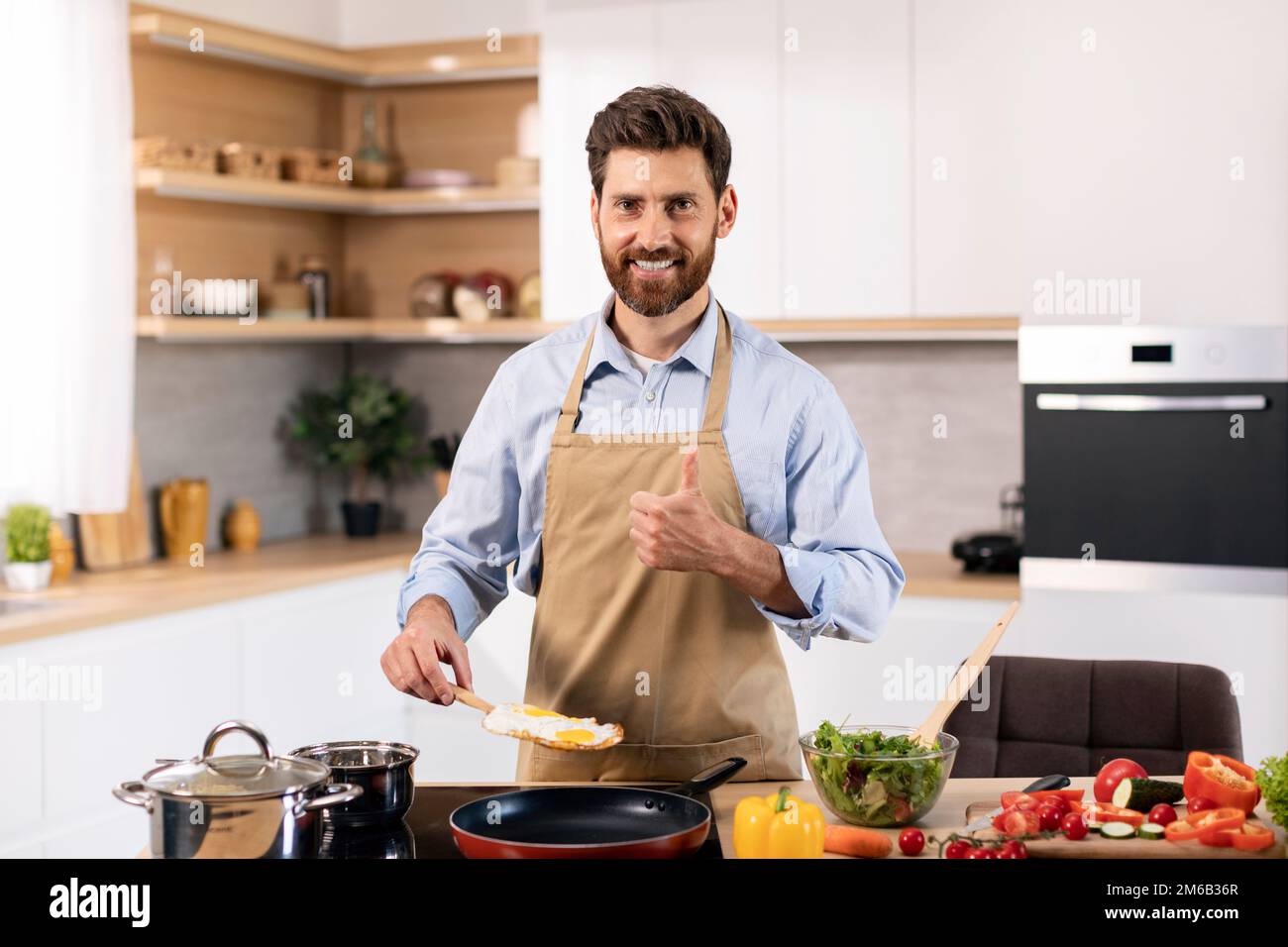 Glad millennial caucasian bearded guy chef in apron preparing scrambled ...