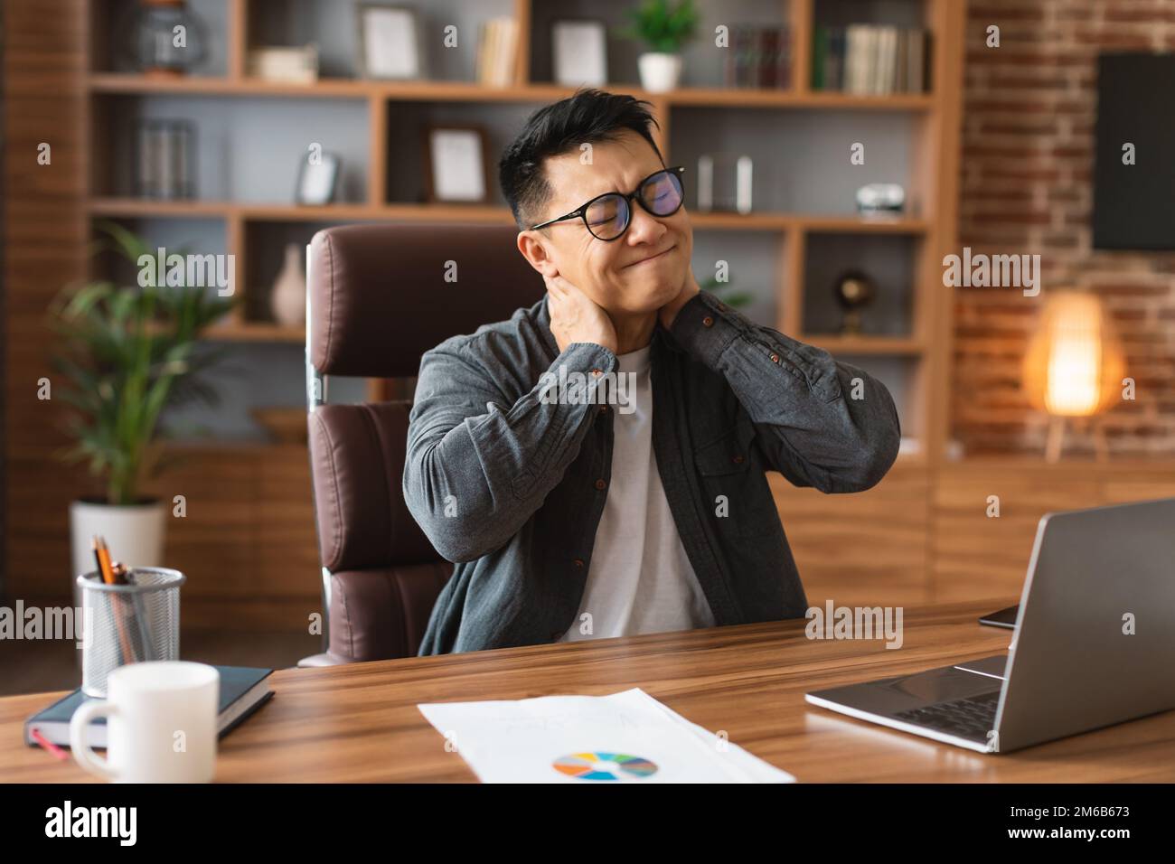 Despaired sad mature japanese male in glasses works on laptop suffers ...