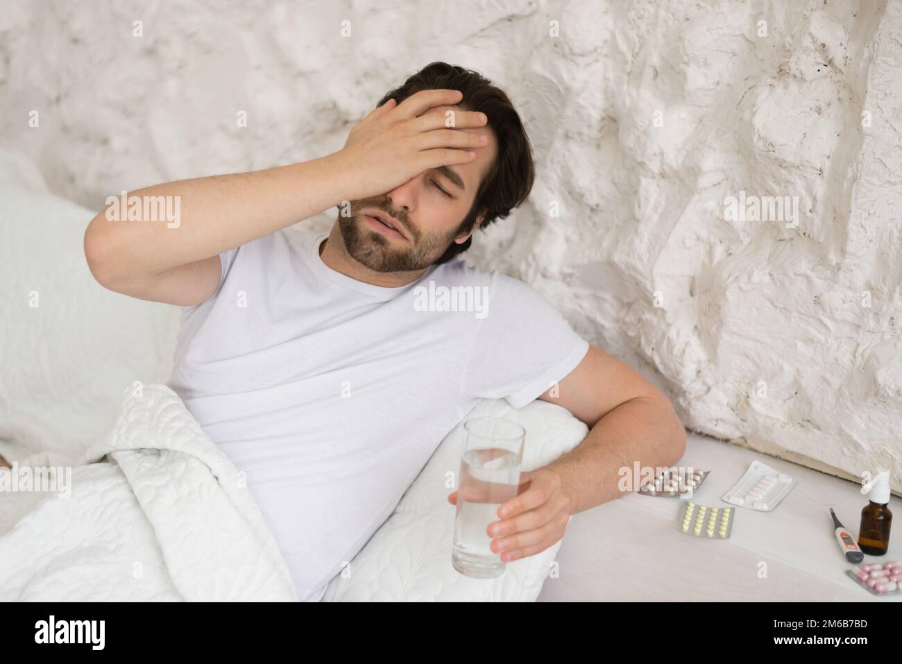 Despaired sad young caucasian man lies on bed with pills, suffers from ...