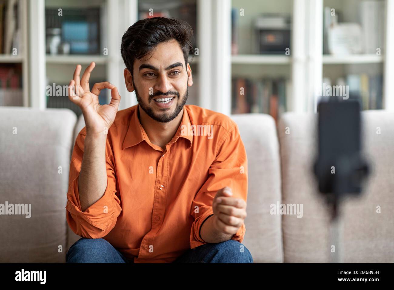 Positive handsome arab guy vlogger streaming from home, using phone ...