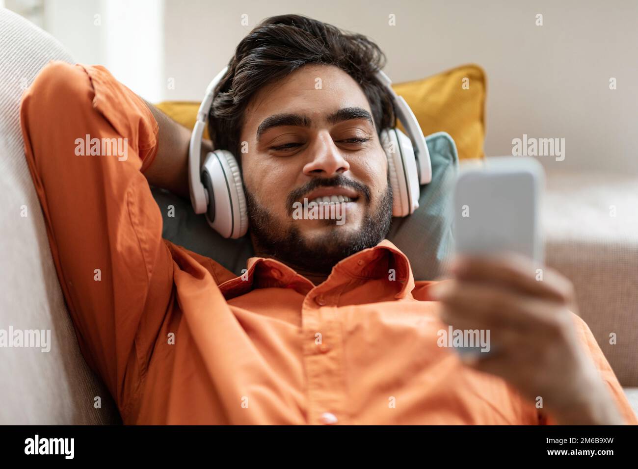 Relaxed arab guy lying on couch with phone and headphones Stock Photo ...
