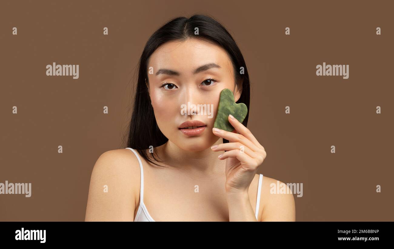 Korean lady massaging face by gua sha quartz stone scraper for skincare ...