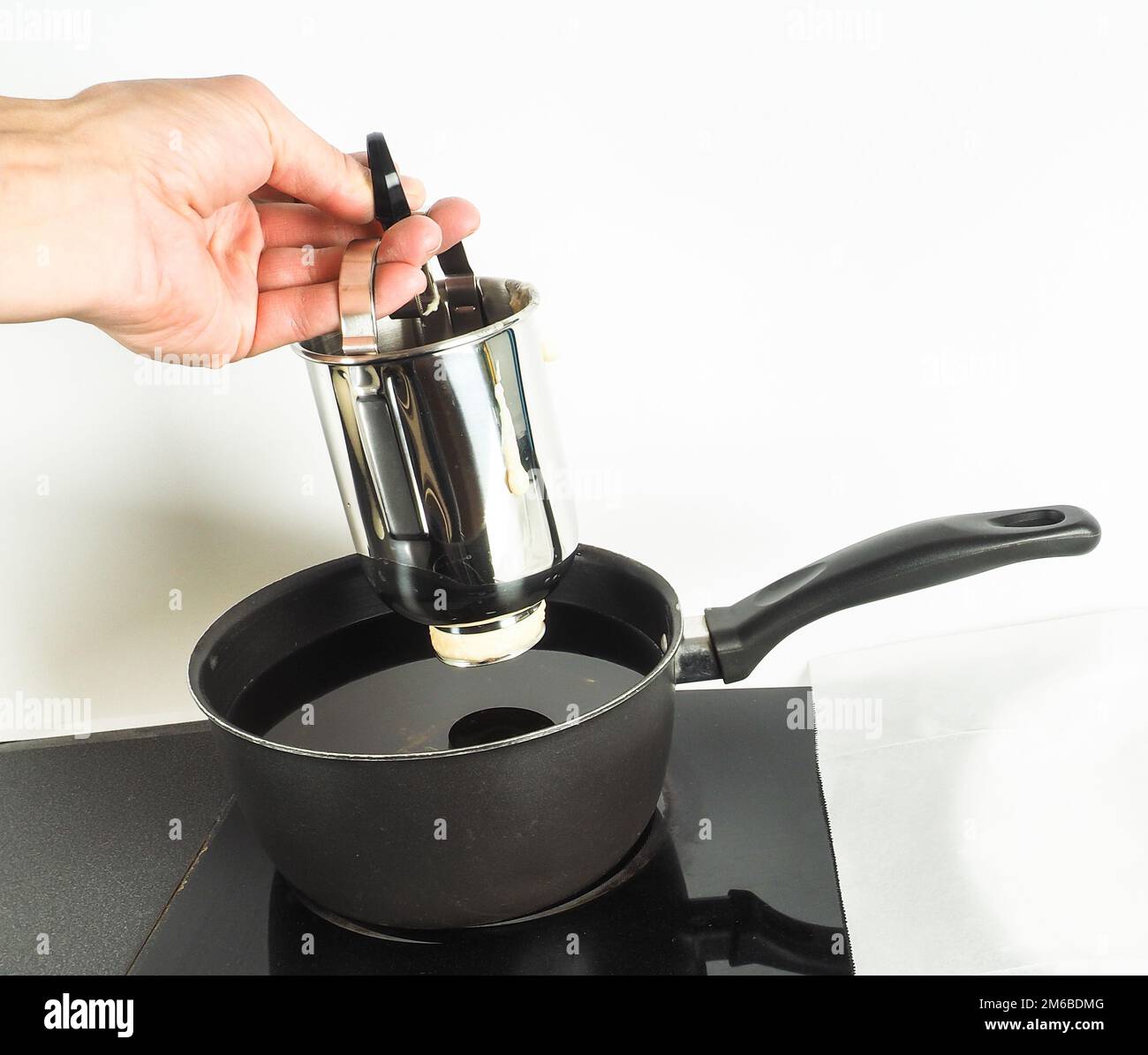 Baker making donuts with a squeeze container into hot oil in small ...