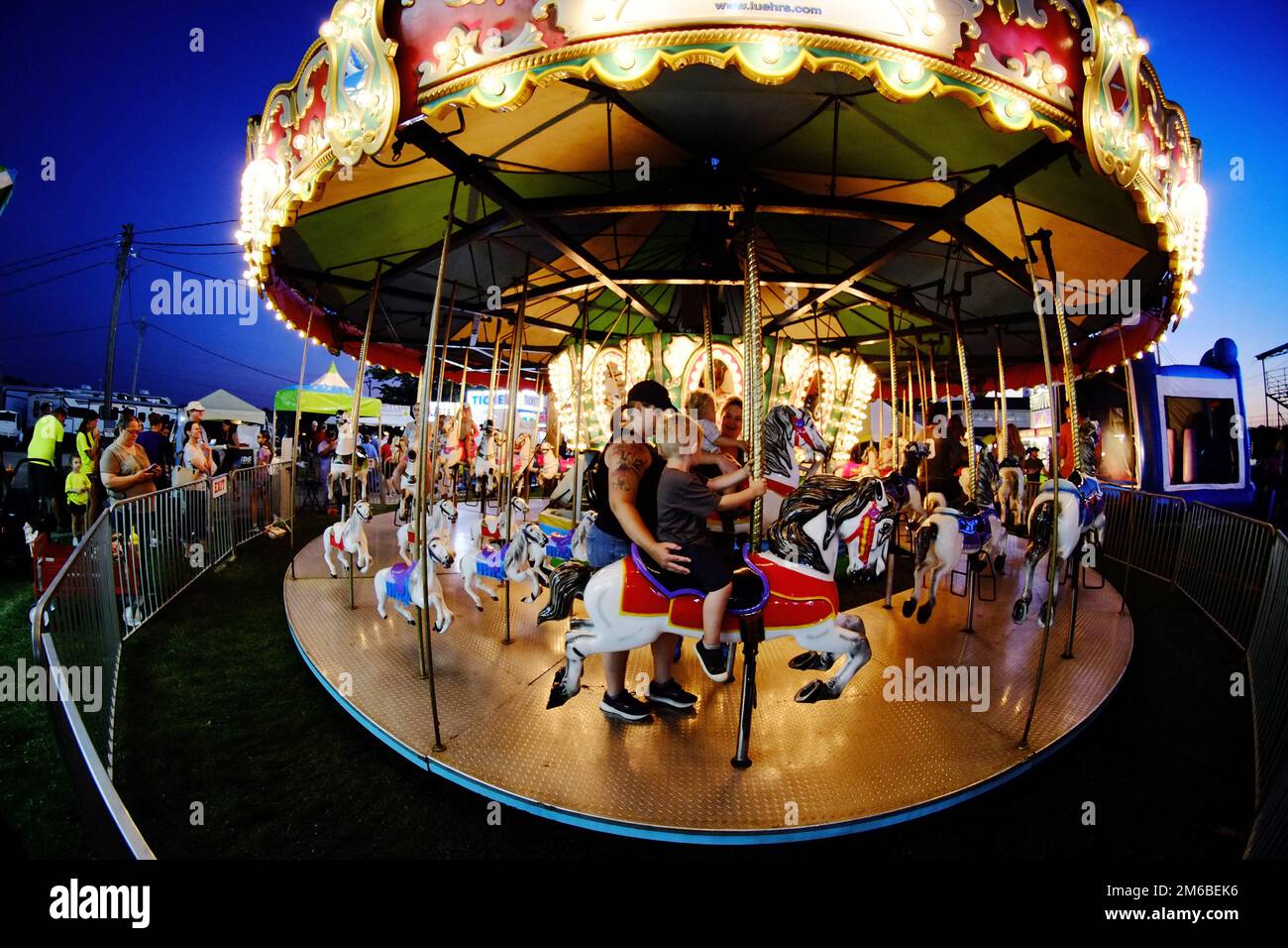 Children and adults ride on a carousel at a carnival on a summer ...