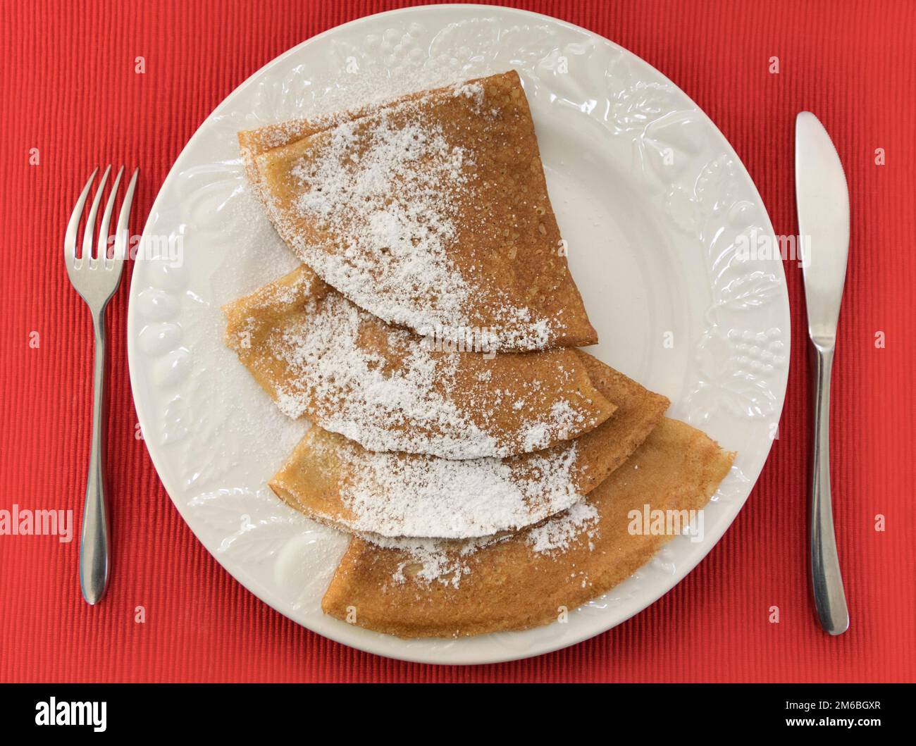 Pancakes with powdered sugar served on a white and red background plate ...