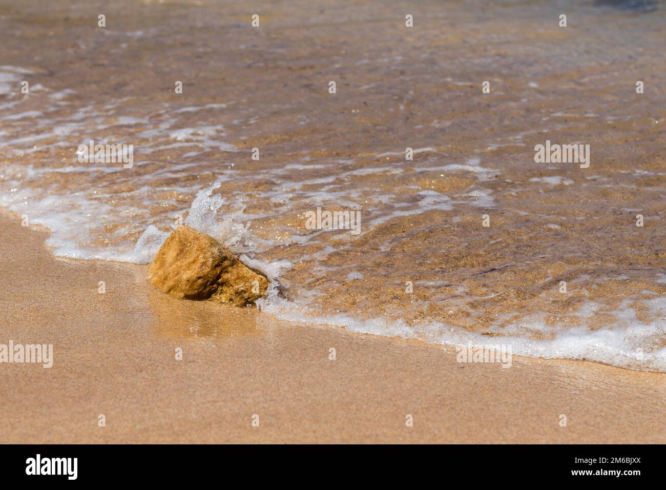 Beautiful crystal clear sea wave splashing over rock on golden sandy ...