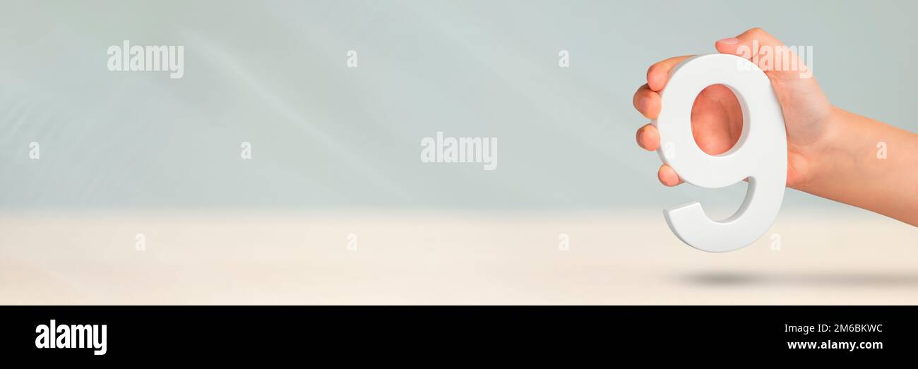 Number nine in hand. A hand holds a white number 9 on a blurred ...