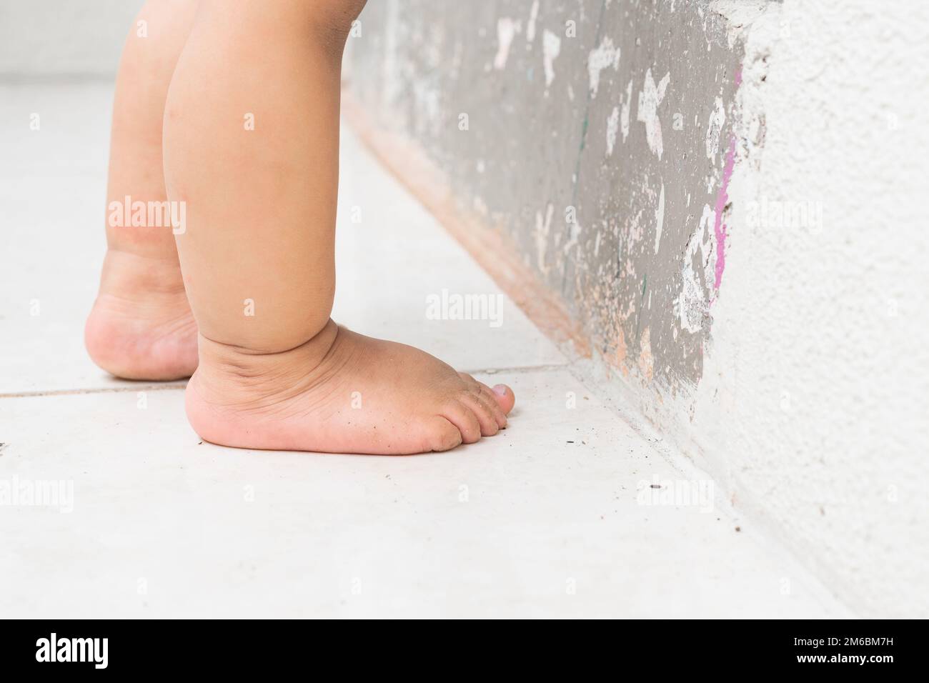 close-up of a brunette baby's feet, standing on a white tile, next to a ...