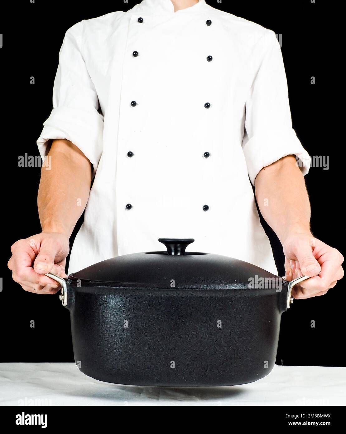 Chef holding a casserole towards, over white table clothing on black ...