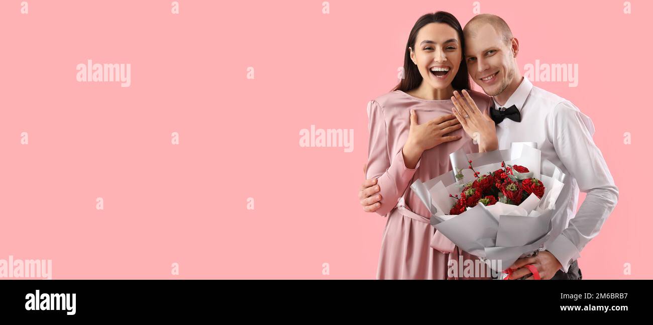 Engaged young couple with bouquet of flowers on pink background with ...