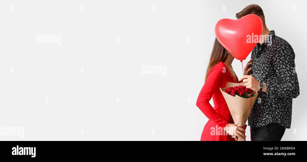 Happy young couple with bouquet of flowers and balloon on light ...