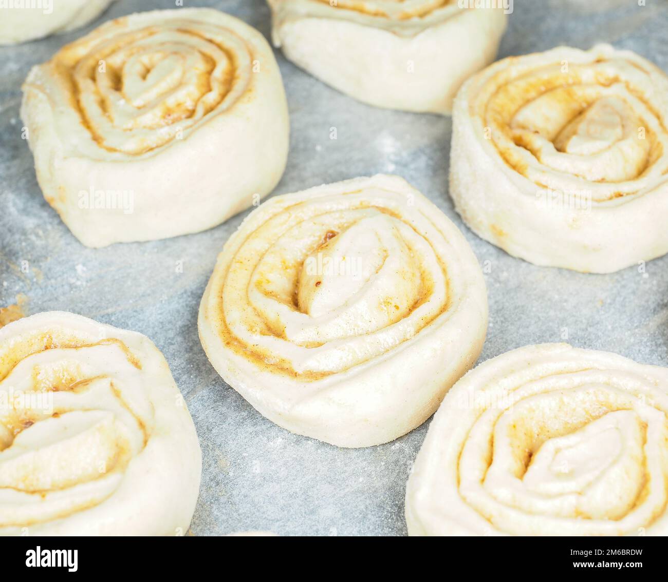 Closeup of raw cinnamon roll and cinnamon buns on baking paper Stock ...