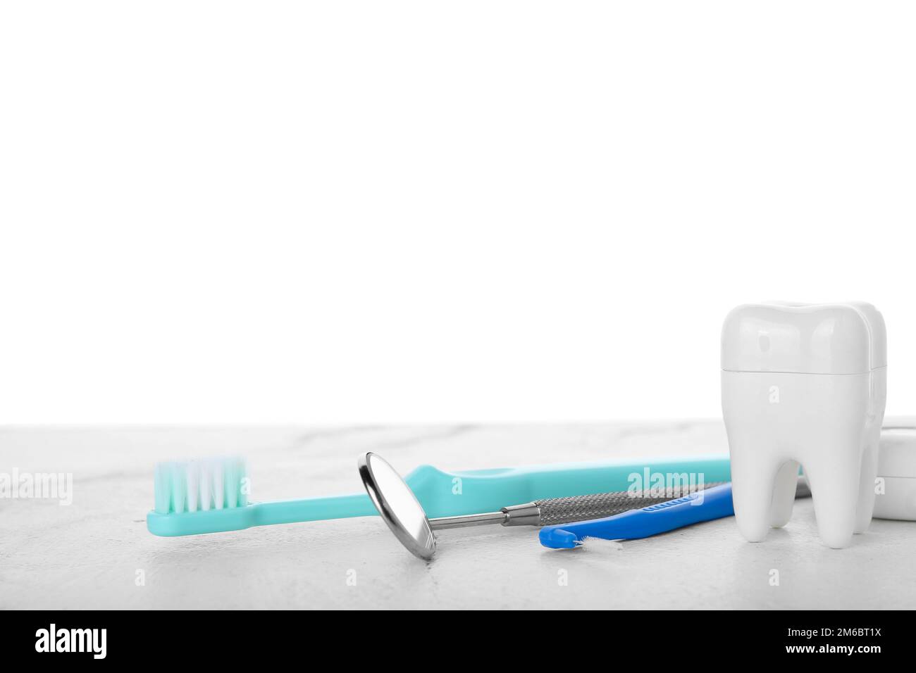 Plastic tooth with dental floss and tools on table against white ...