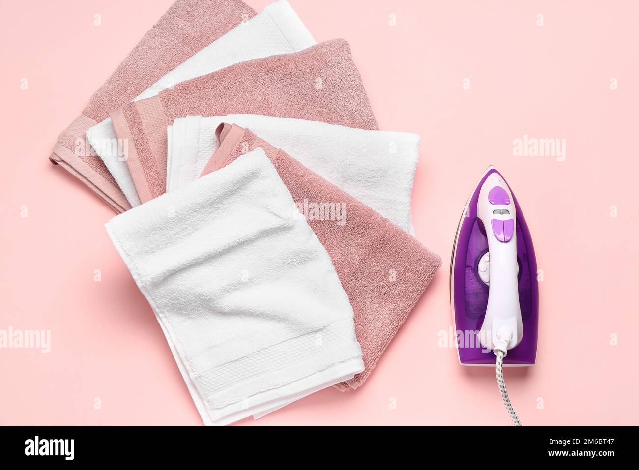 Stack of towels and electric iron on light pink background Stock Photo ...