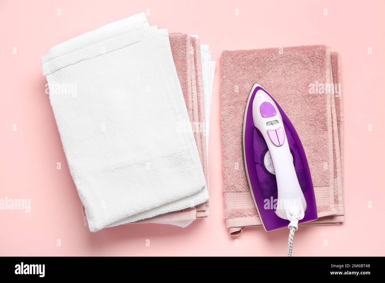 Stack of towels and electric iron on light pink background Stock Photo ...