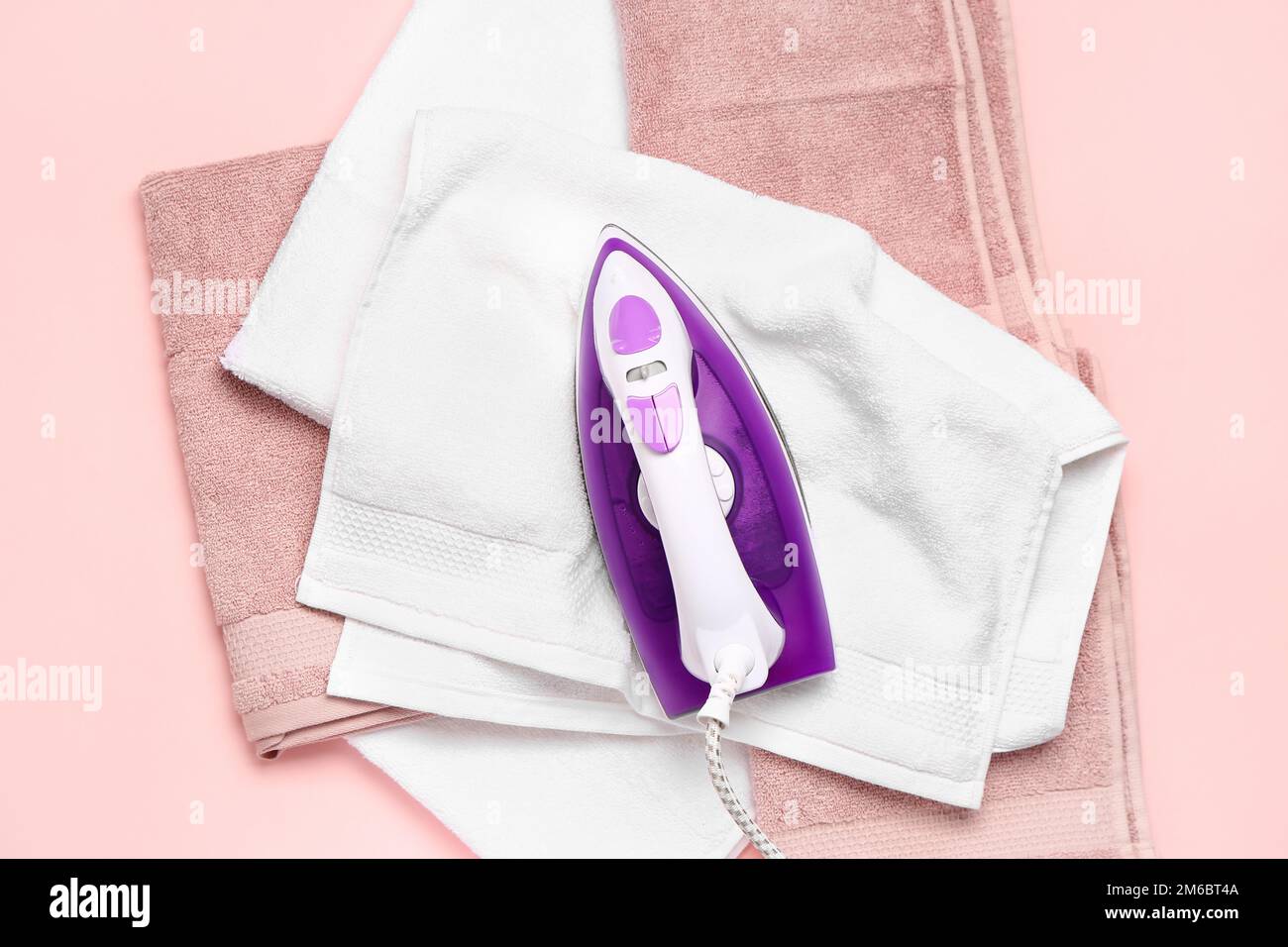 Stack of towels and electric iron on light pink background Stock Photo ...
