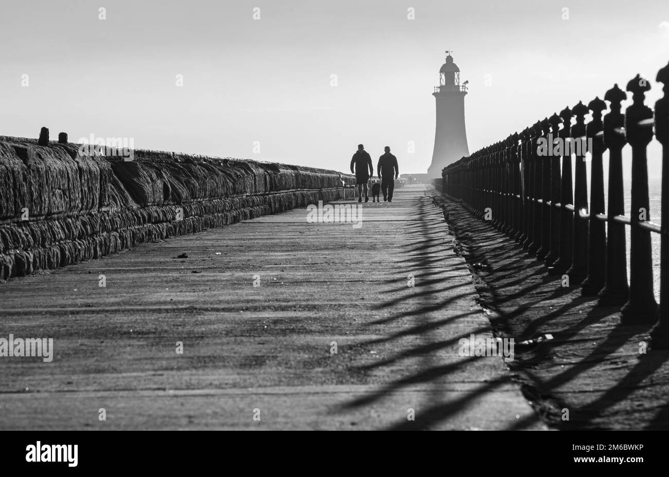 A grayscale of silhouettes walking on the Tynemouth Pier with the ...