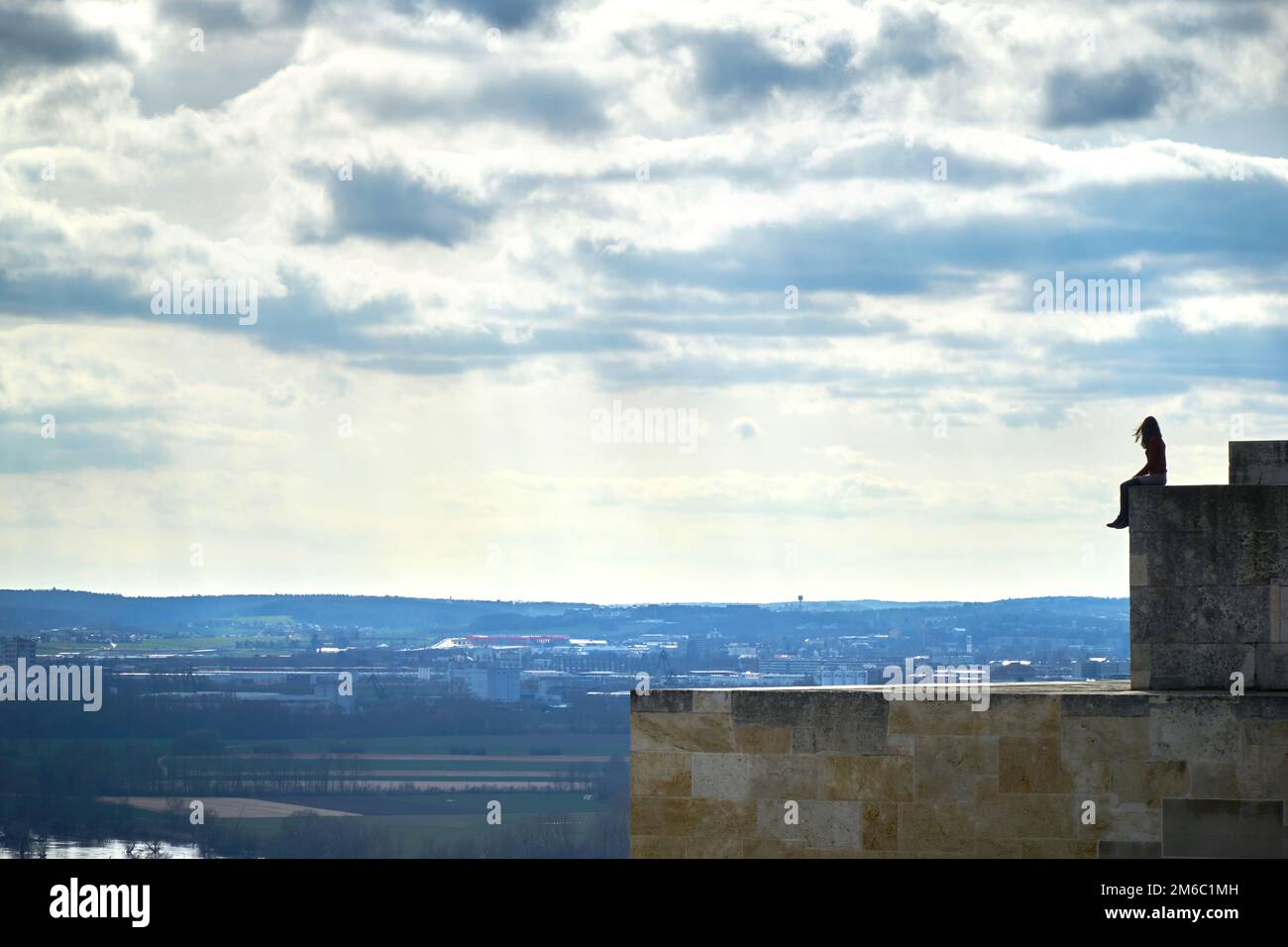 Young woman is looking into the landscape on a terrace with dramatic ...