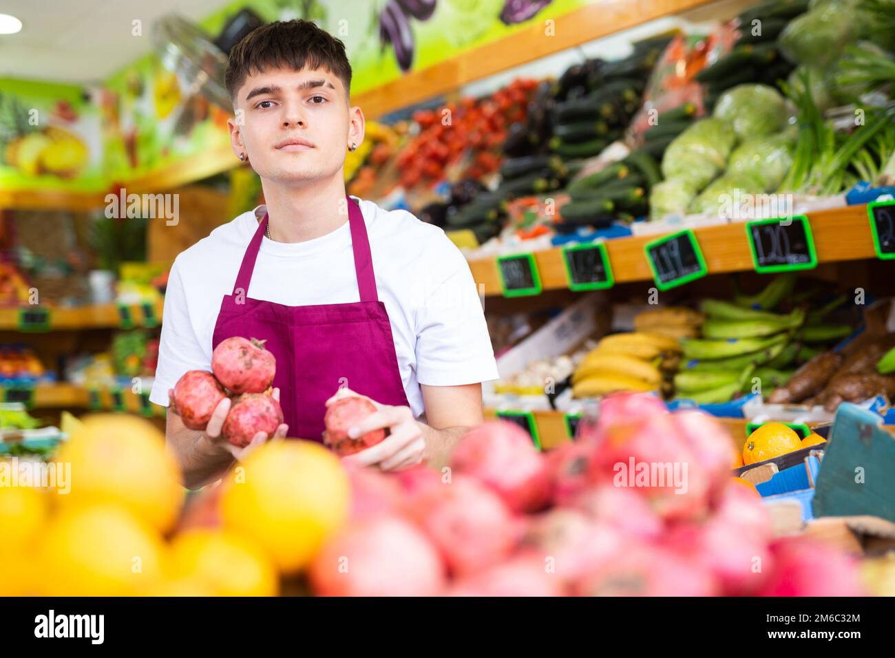 Male employee of a grocery store laying out pomegranate fruit on ...