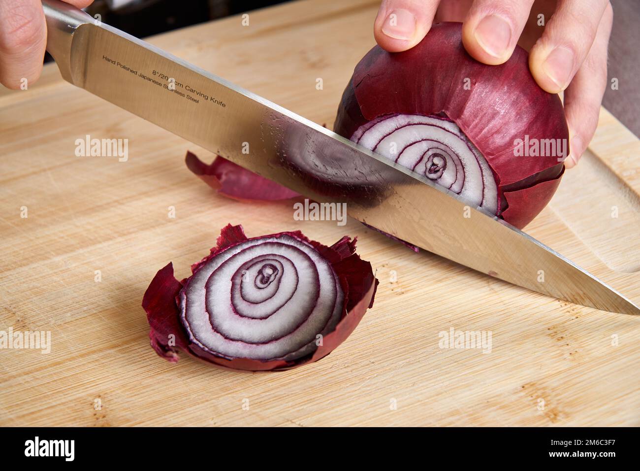 View on hands of a man chopping fresh red onion for lunch an a bamboo ...