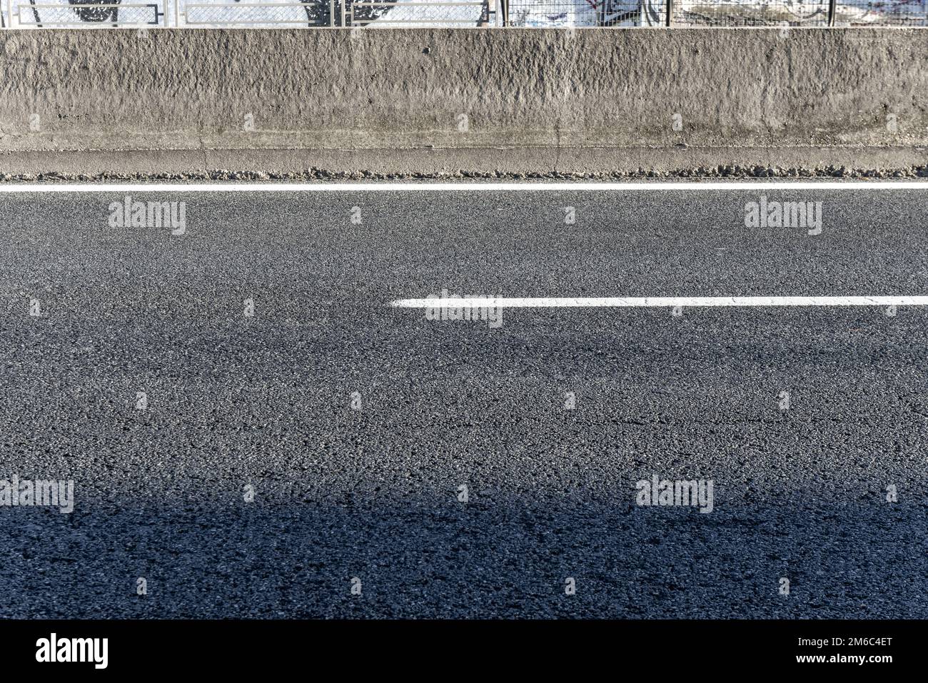 Asphalt of a road with white paint separating the lanes and a concrete ...