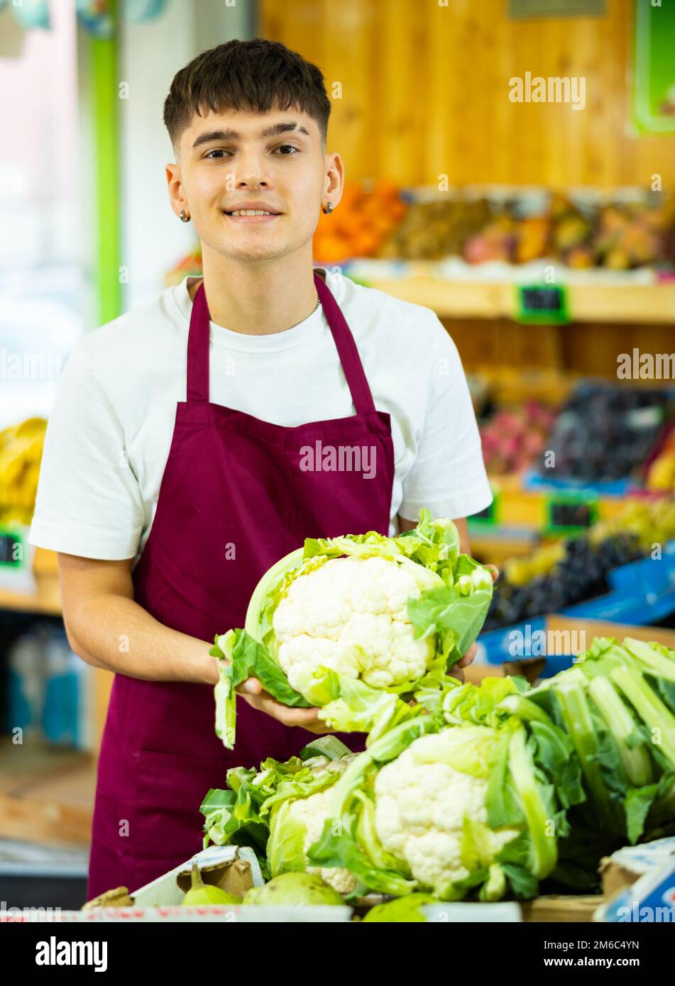 Portrait of joyful male merchandiser with cauliflower in hands at ...