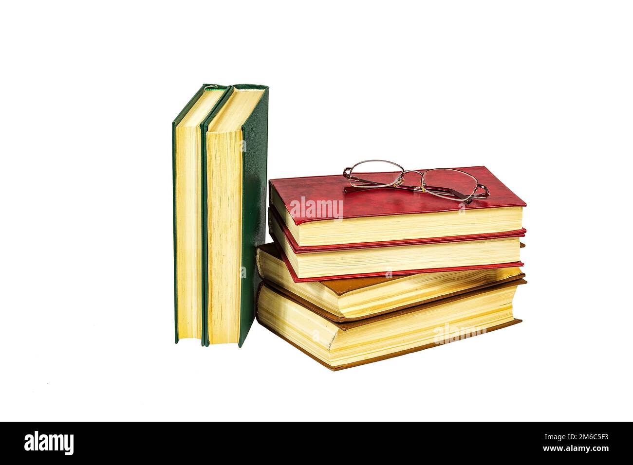 On the white surface is a pile of hard-bound books and reading glasses ...