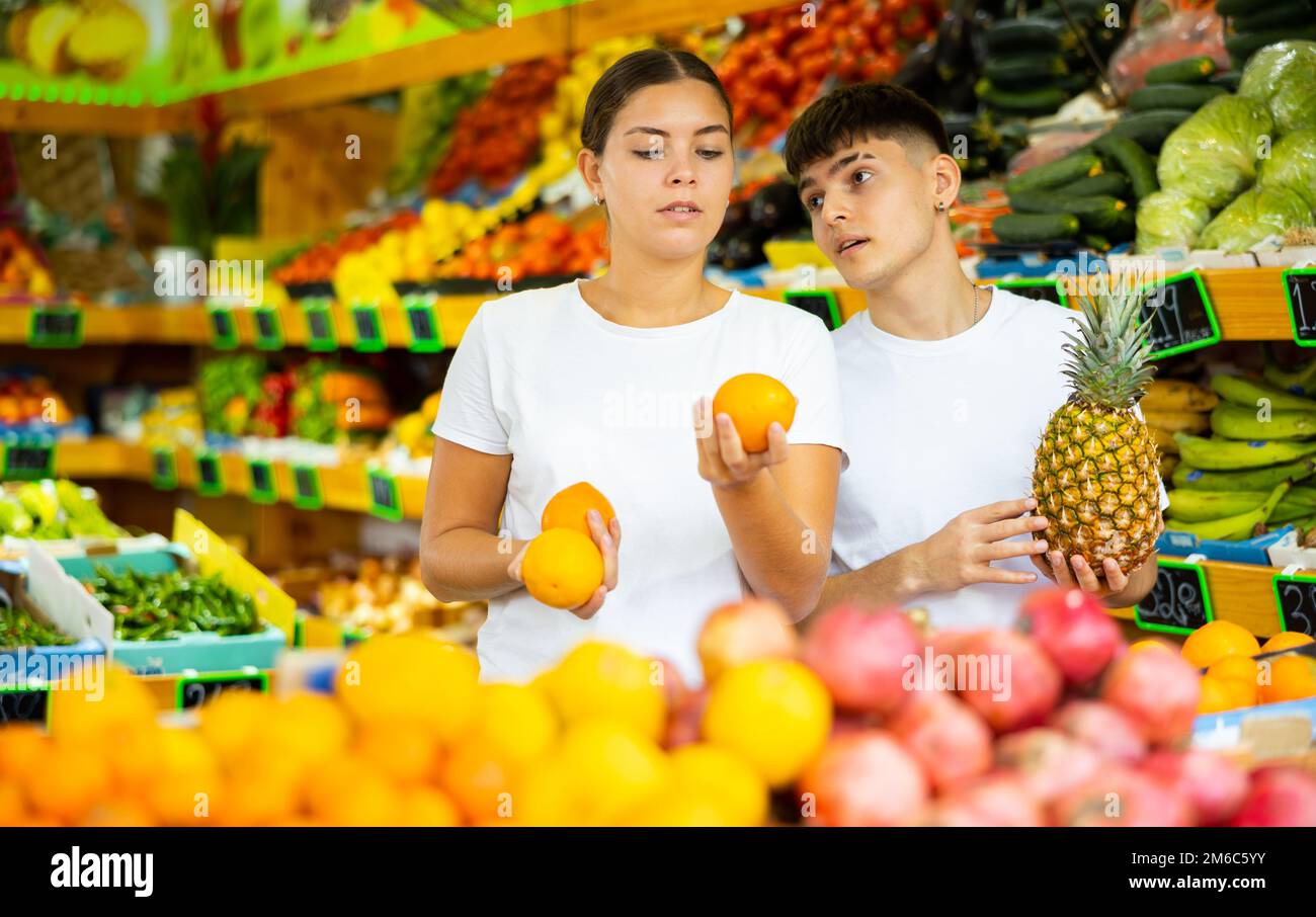 Young positive couple choosing fresh pineapples and oranges tropical ...