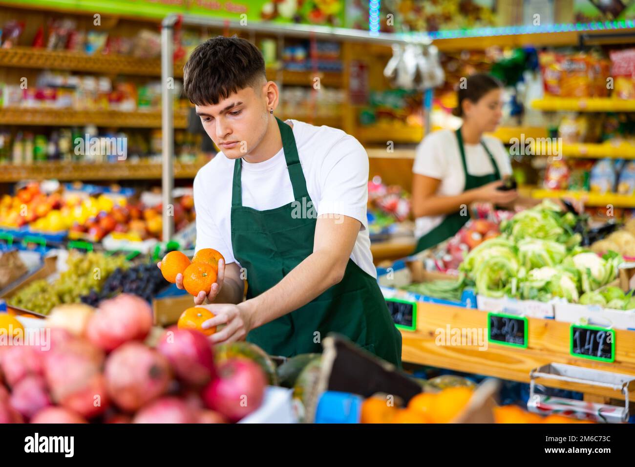 Professional young male supermarket worker in green apron arranging ...