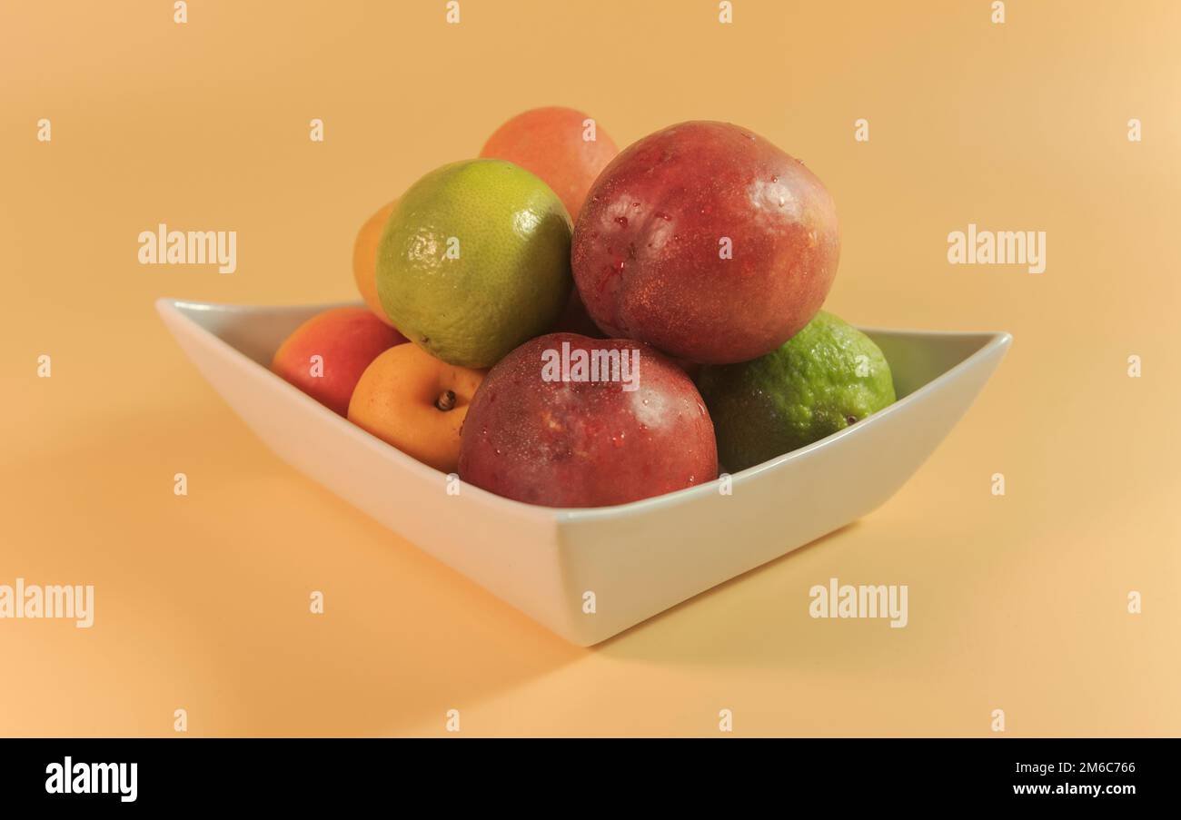 Fresh natural fruits in a white corner plate on a peach background ...