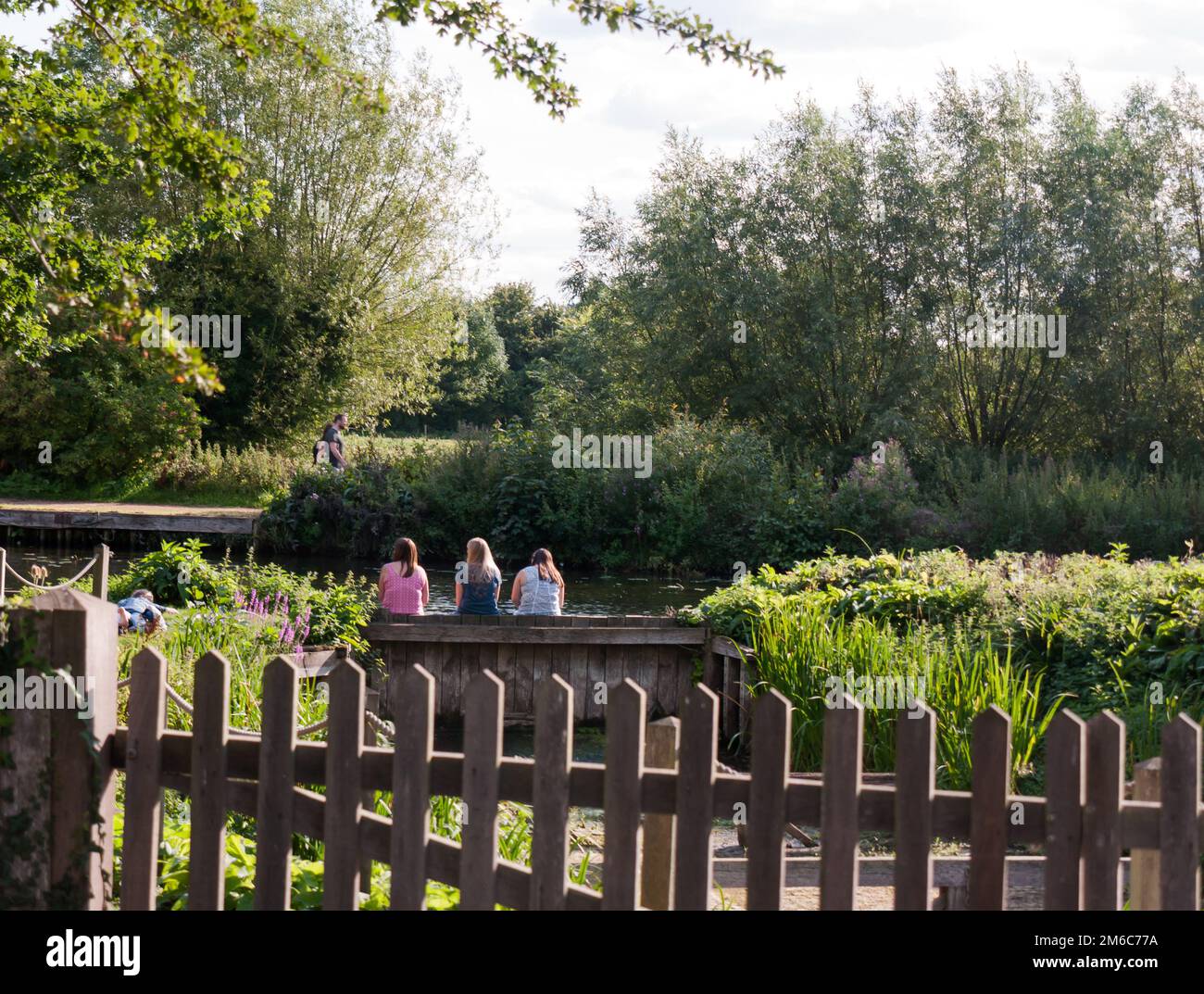 Three women sitting on a wall behind fence on a summer's day Stock ...