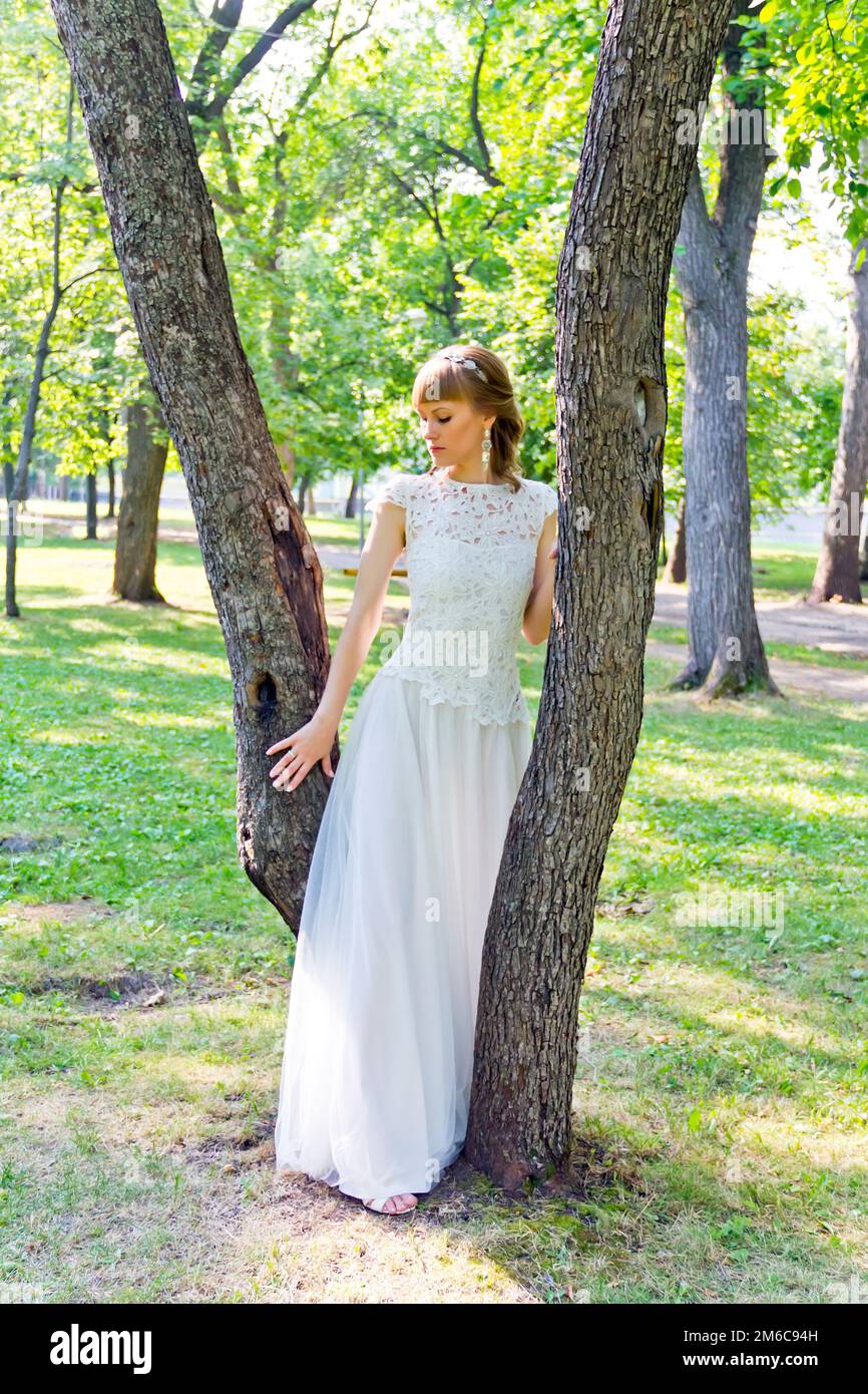 Bride in white lace dress standing near tree Stock Photo - Alamy