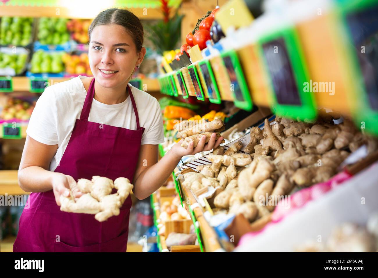 Happy young female seller puttingginger on shelves in grocery shop ...