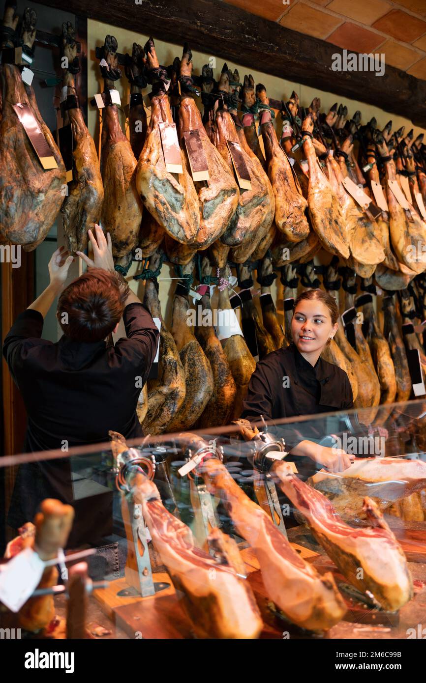 Young female and male vendors arranging jamon at counter in butcher ...