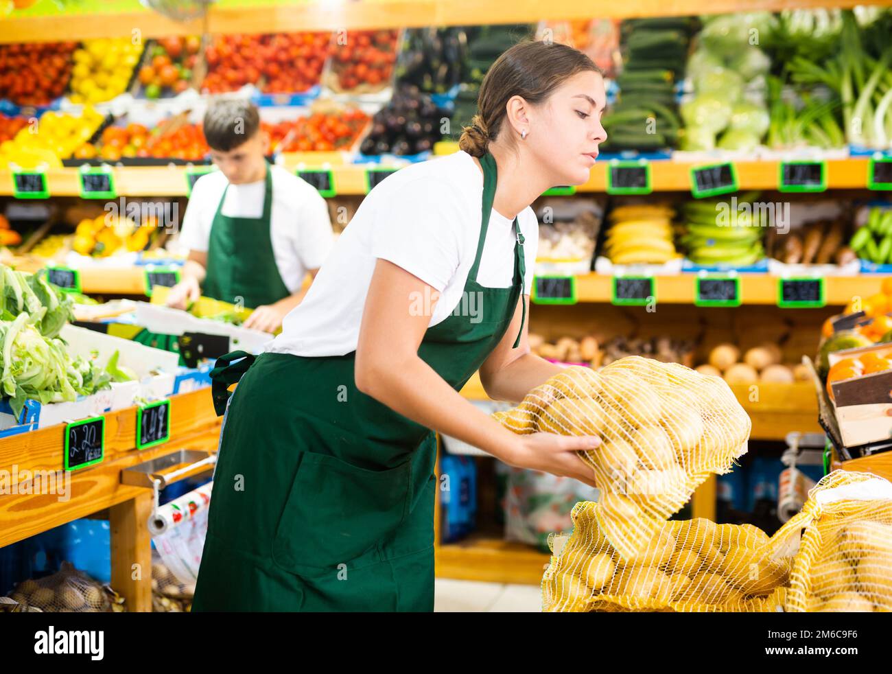 Female shop assistant lays potatoes on counter in grocery shop Stock ...