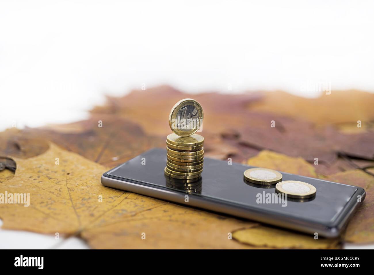Smartphone on maple leaves background with some coins Stock Photo - Alamy