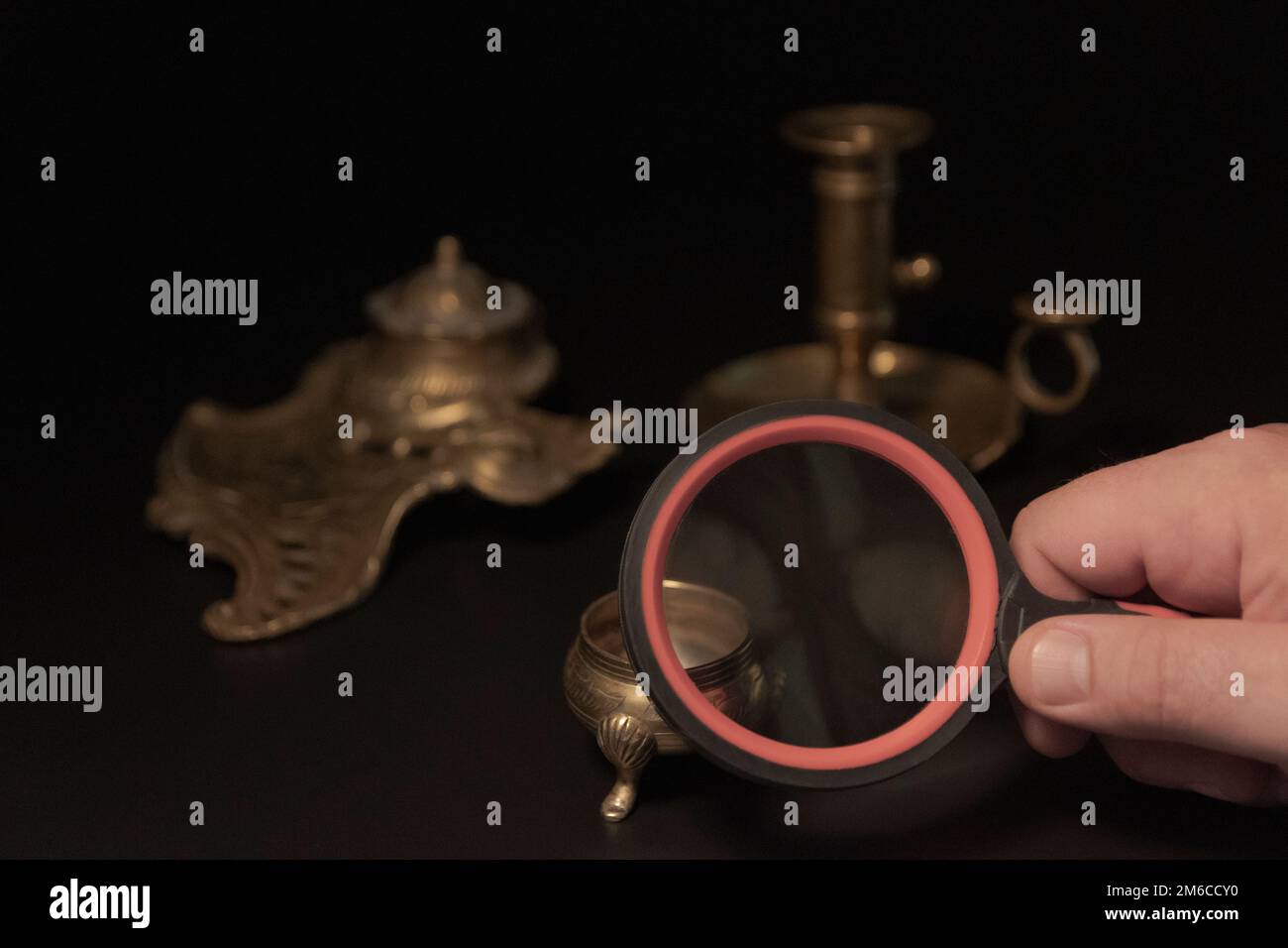 Hand with a magnifying glass while examining antique items. Expertise ...