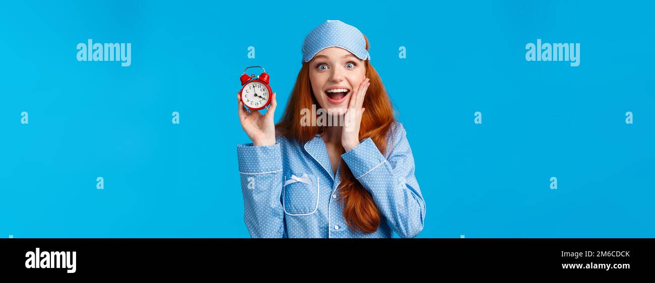 Excited young girl wake up on time, holding red cute clock set alarm ...