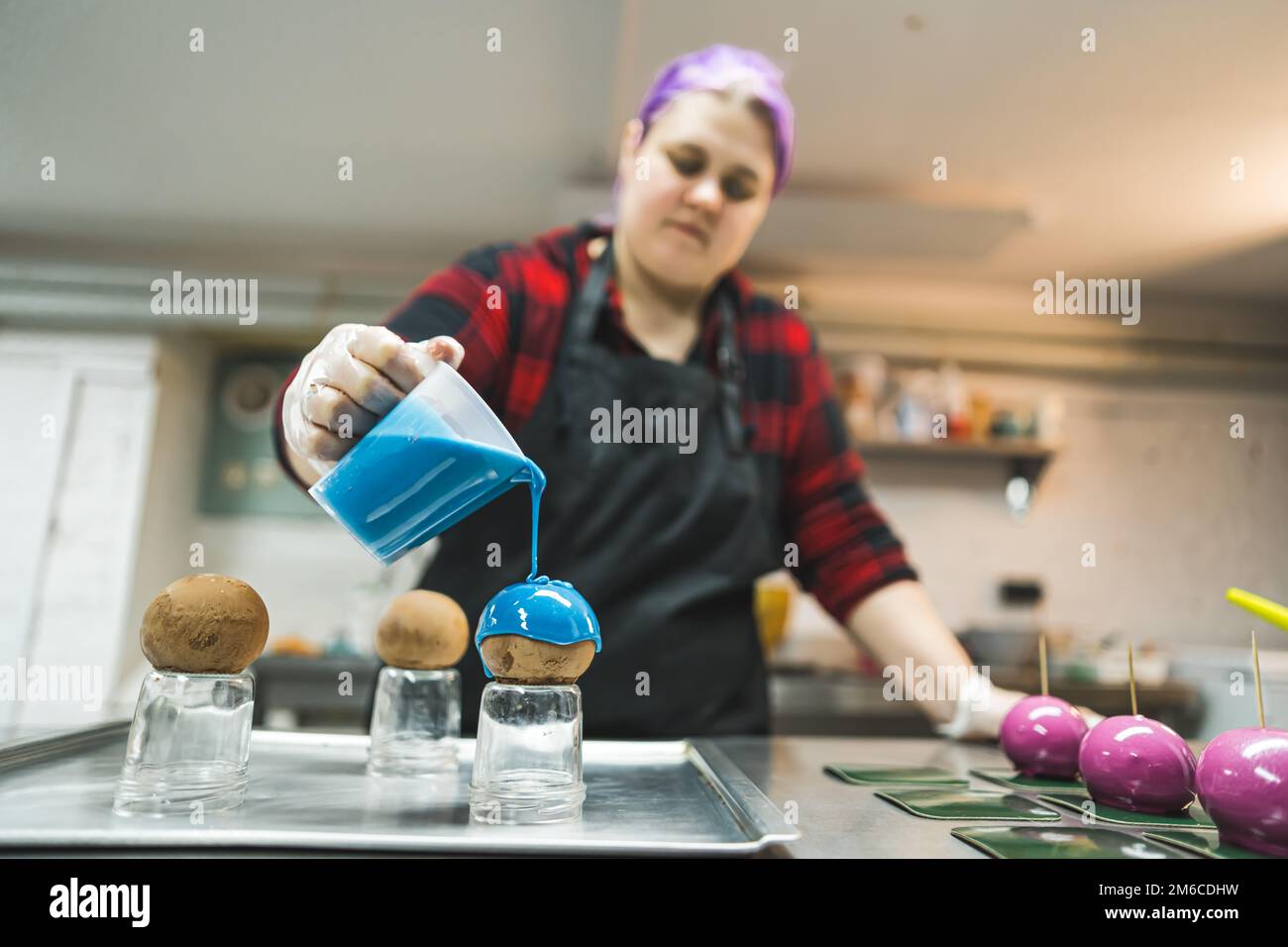 Decorating process. Woman pastry chef pouring blue icing onto pralines ...