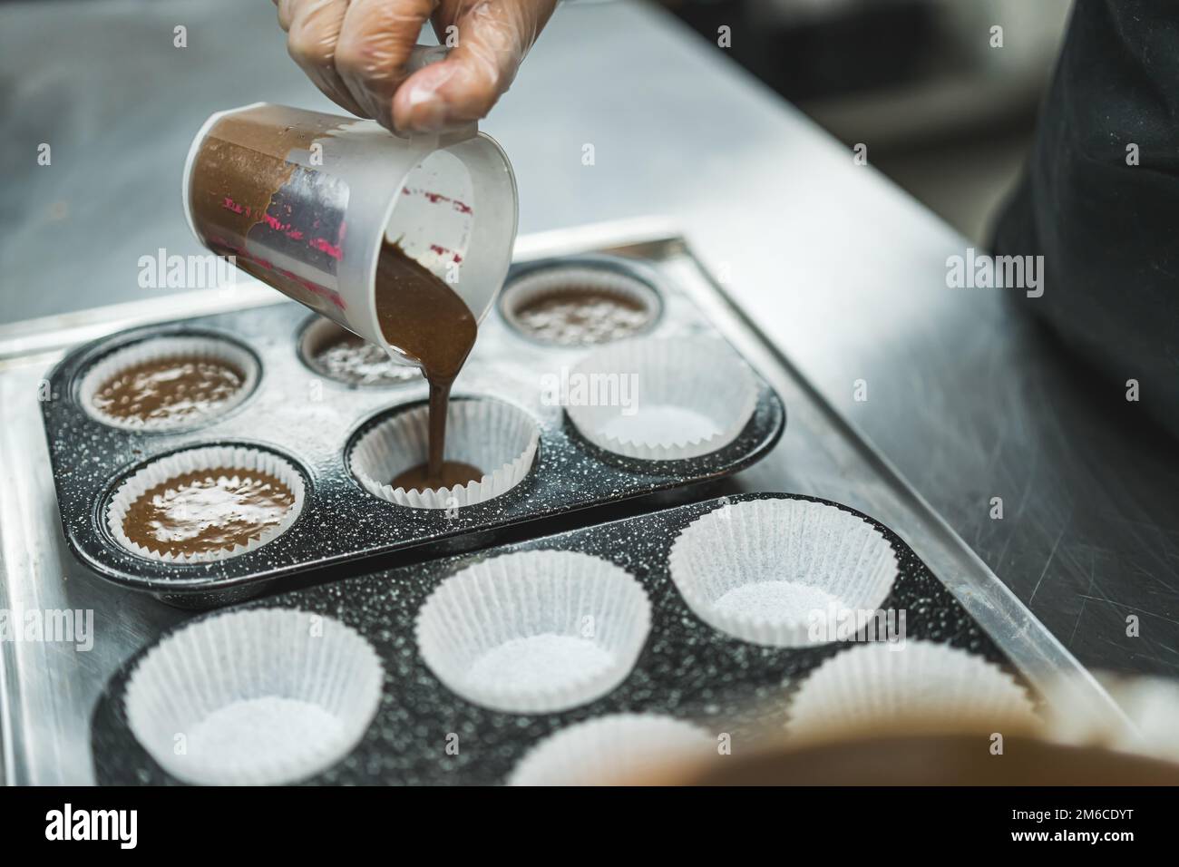 Side view of chocolate dough being poured into cupcake liners in two ...