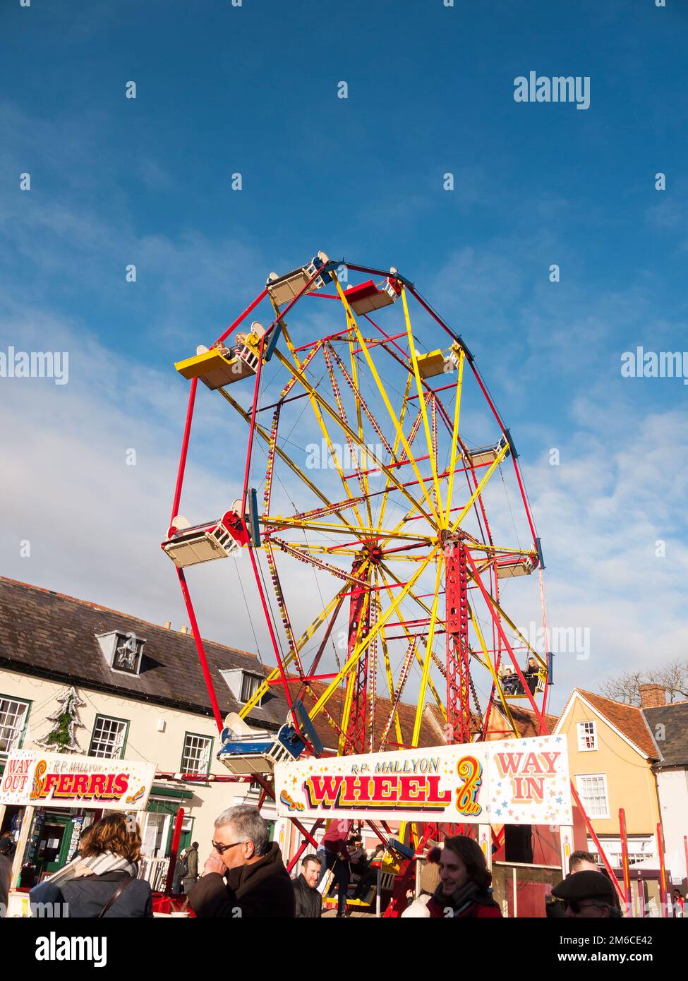 Red and yellow carousel wheel outside with people below blue sky ...