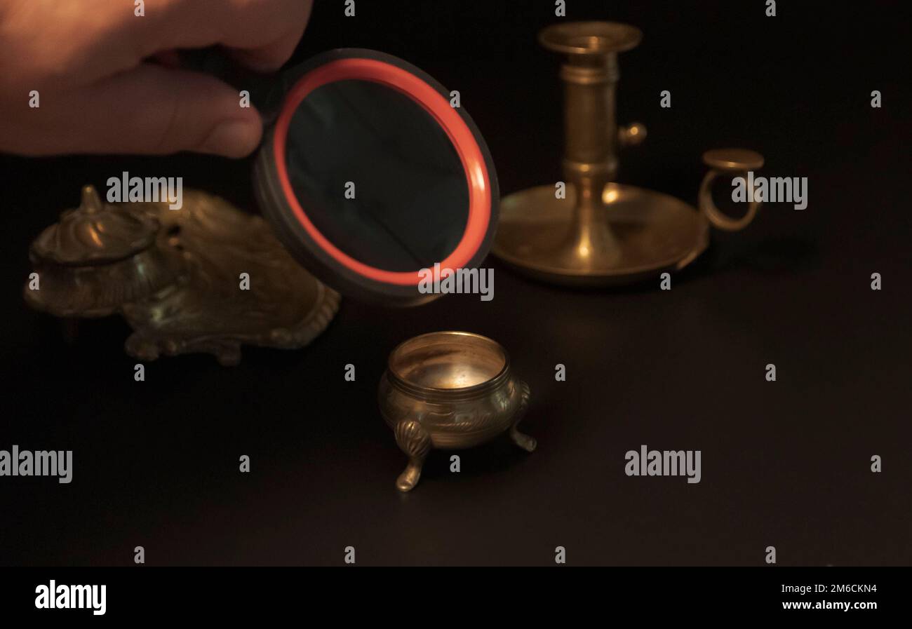 Hand with a magnifying glass while examining antique items. On black ...