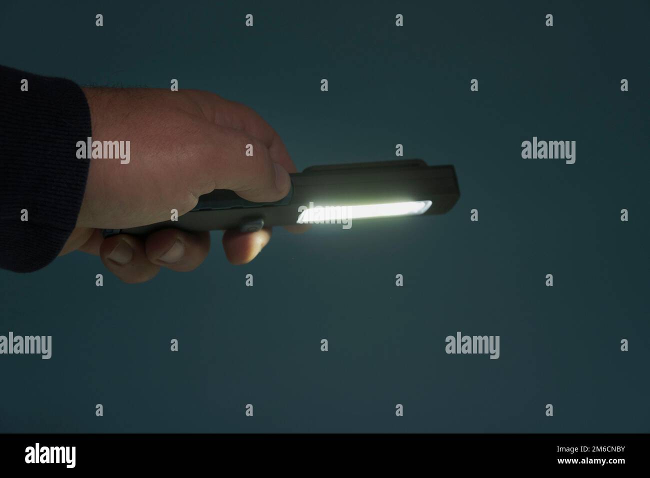 Pocket led flashlight in hand. illuminates blue background. Copy space ...