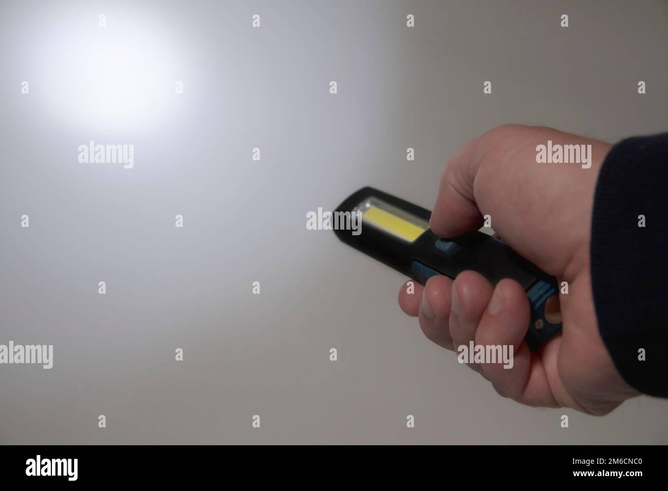 Pocket led flashlight in hand. illuminates gray background. Copy space ...