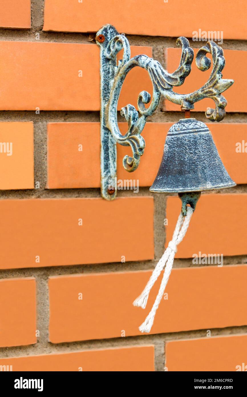 An ancient bronze bell with a rope on a red brick wall of a rich house ...