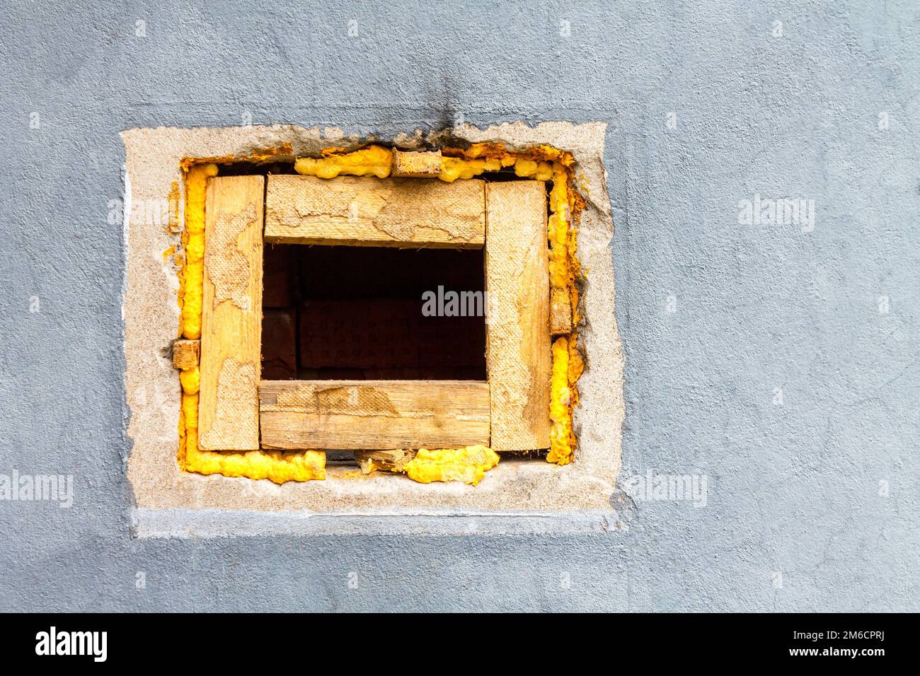 A square hole with wooden blocks in a brick wall painted with gray ...
