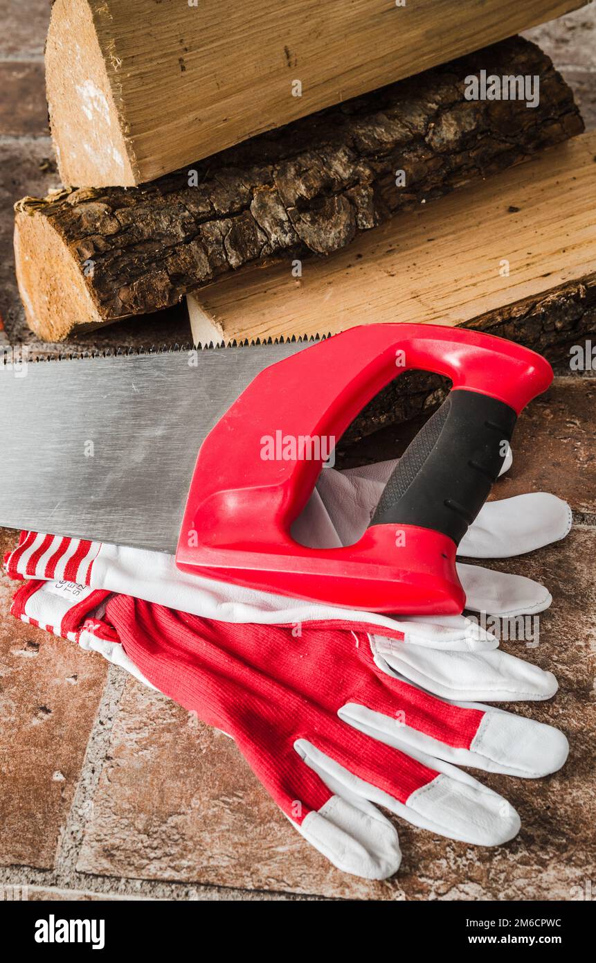 Saw, mittens and firewood, close-up Stock Photo - Alamy