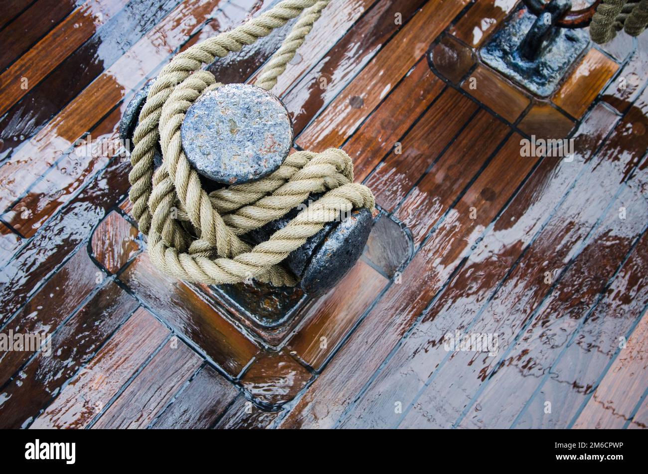 Bollard with a rope on the wooden deck of a sailing vessel, close-up ...