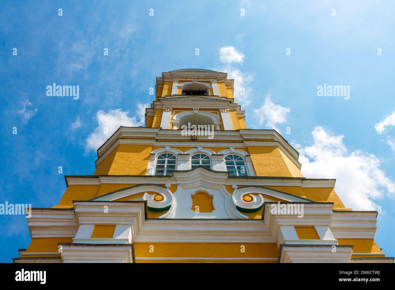 Yellow tower of the Christian temple against the blue sky with white ...
